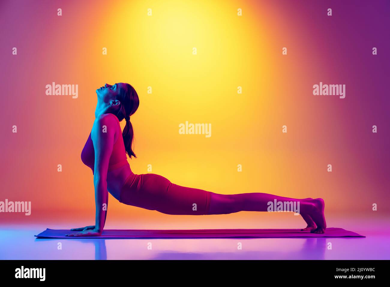 Portrait of young flexible girl training isolated over gradient pink ...
