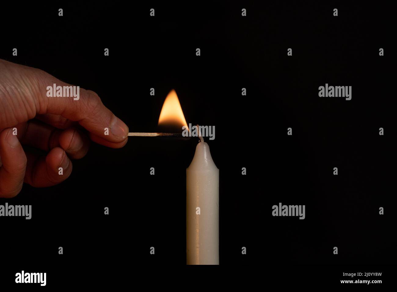 Person's hand holding a matchstick lighting a white candle on a black ...
