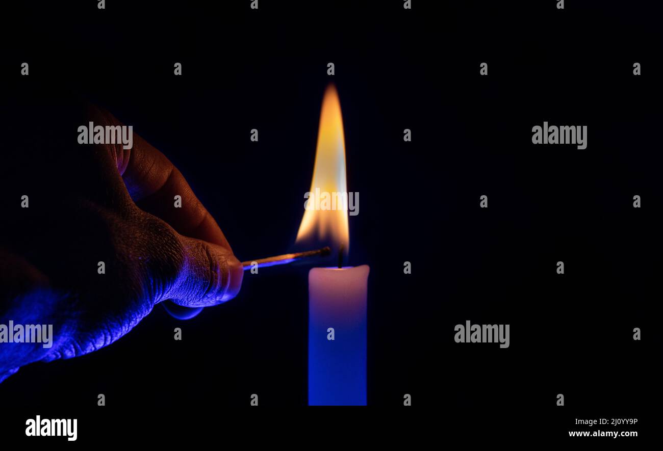 Person's hand holding a matchstick lighting a white candle on a black ...