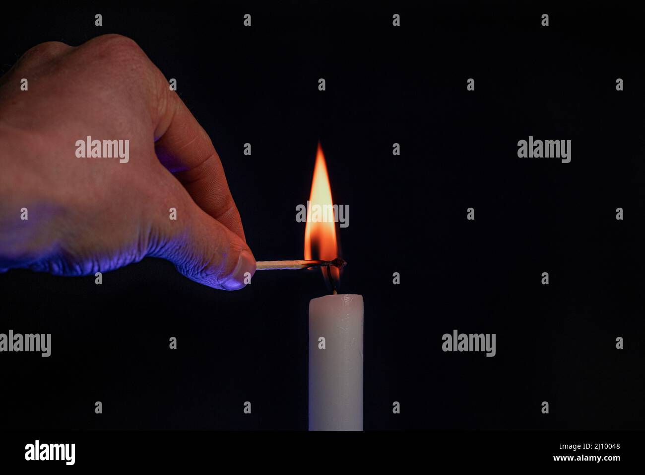 Person's hand holding a matchstick lighting a white candle on a black ...