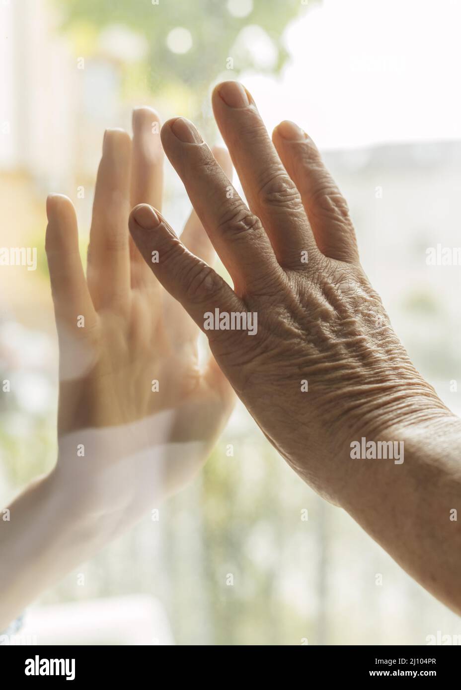 Elder woman touching hand with someone through window during pandemic ...