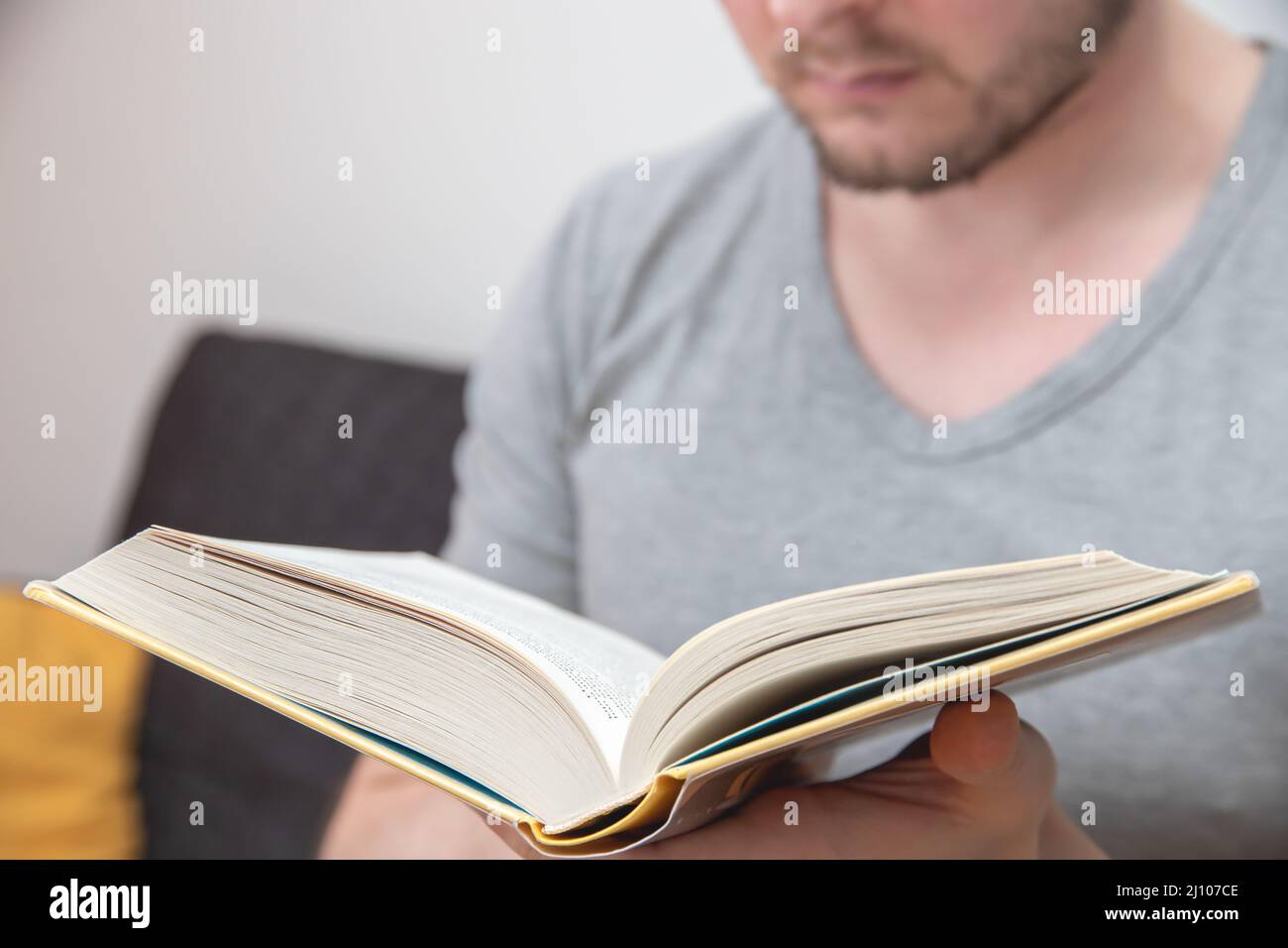 Young male reading a book sitting on the couch Stock Photo - Alamy