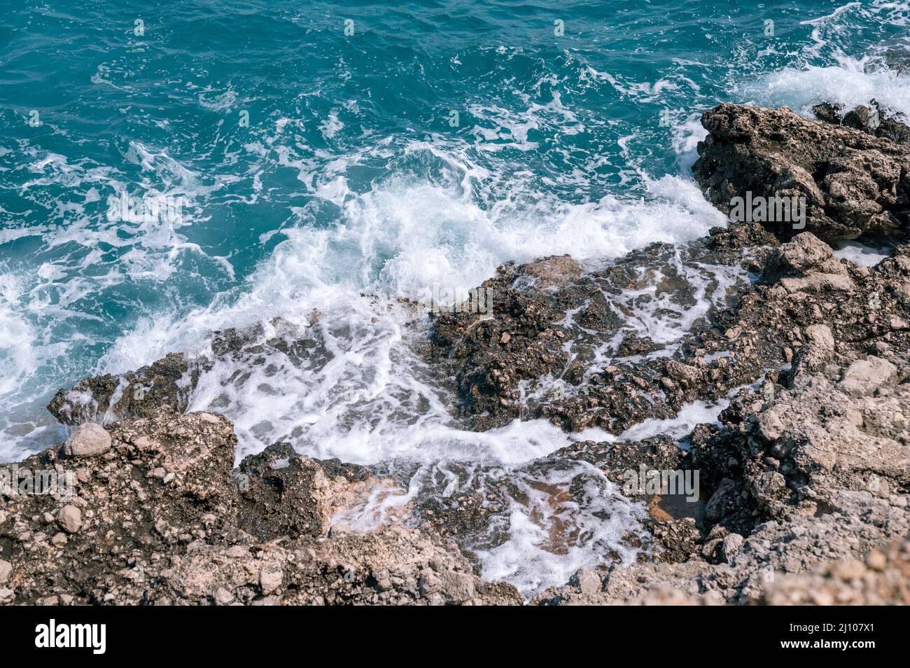 foamy waves of clear blue sea water beat against the rocky shore of the ...