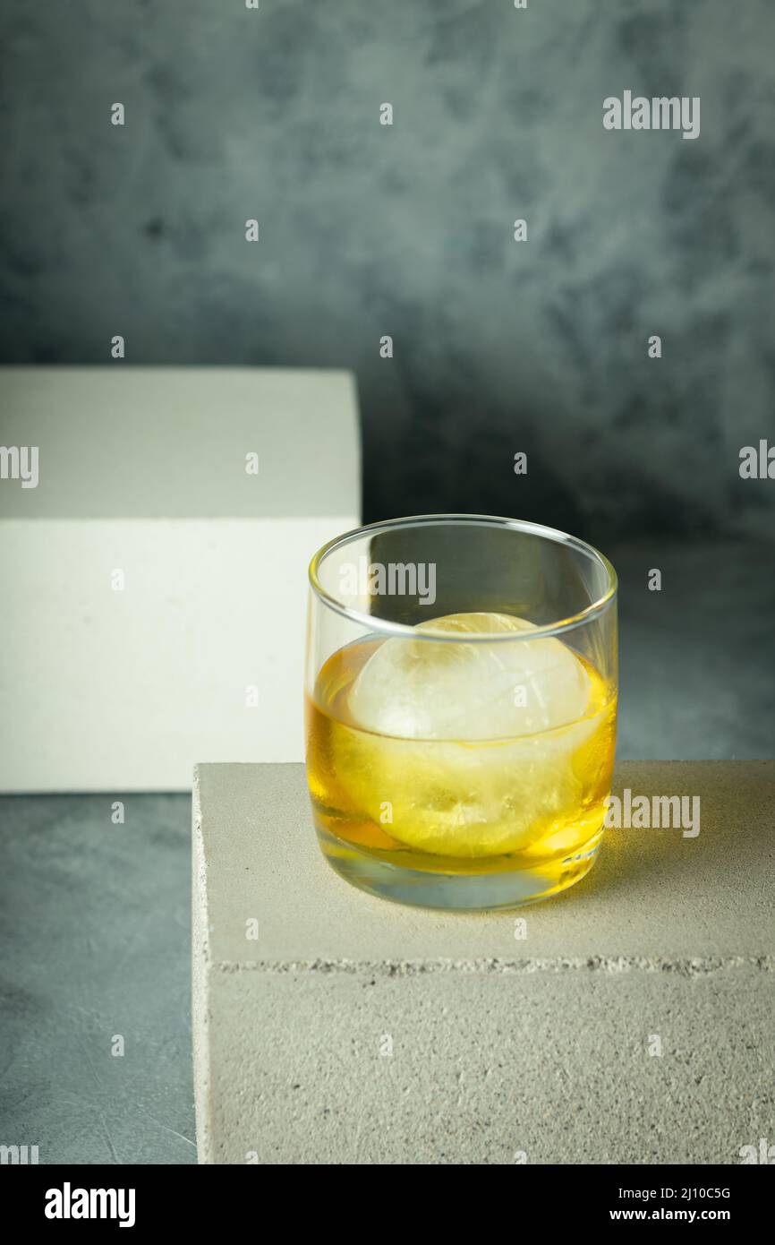 Vertical shot of a cup of single malt scotch whisky with an ice cube on ...