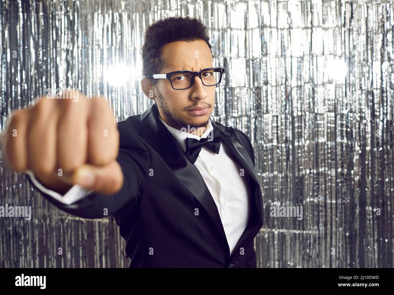 Serious angry young man in a tuxedo, bowtie and glasses holding out his ...
