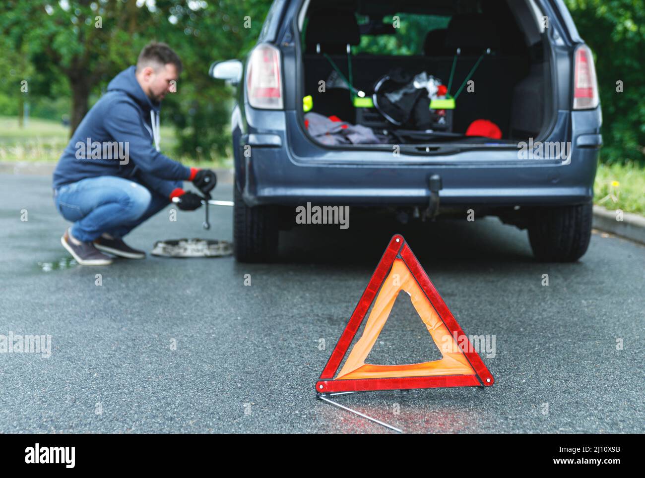 Warning triangle and man changing car wheel Stock Photo - Alamy
