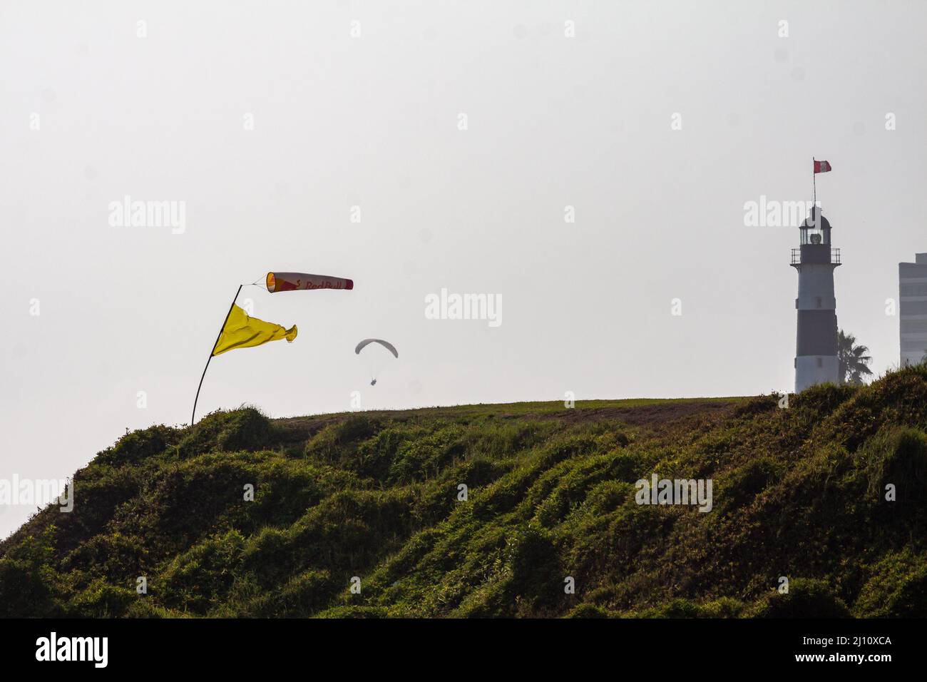Grassy hill with a wind cone, lighthouse and a paraglider flying in ...