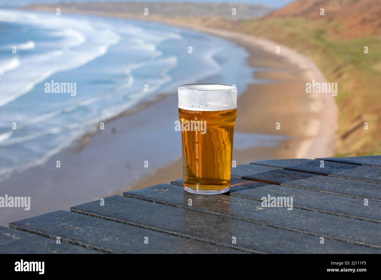 A partly drunk pint of beer on a table overlooking Rhossili Bay and ...