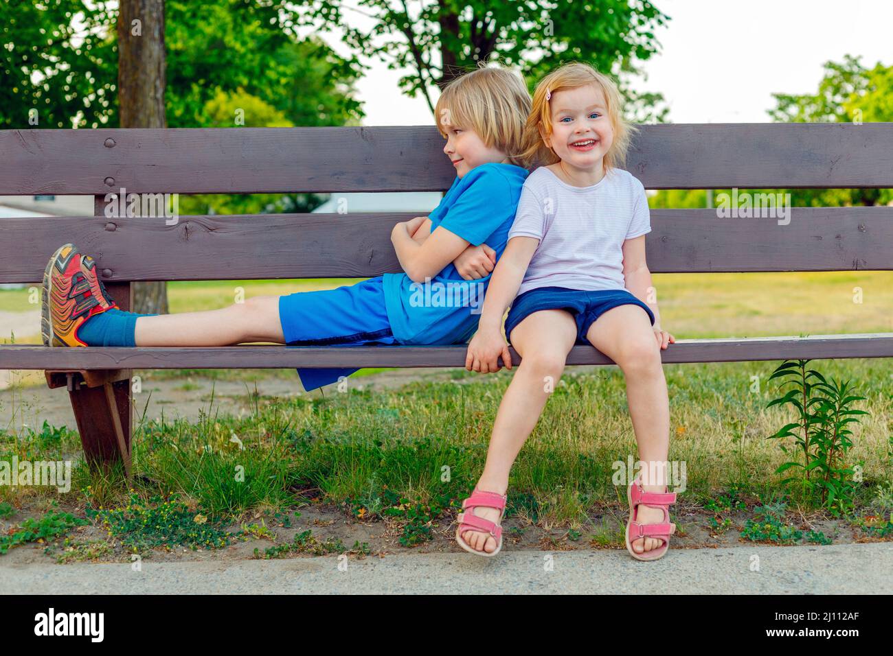 Children sitting on a bench in park in summer. Happy kids having fun ...