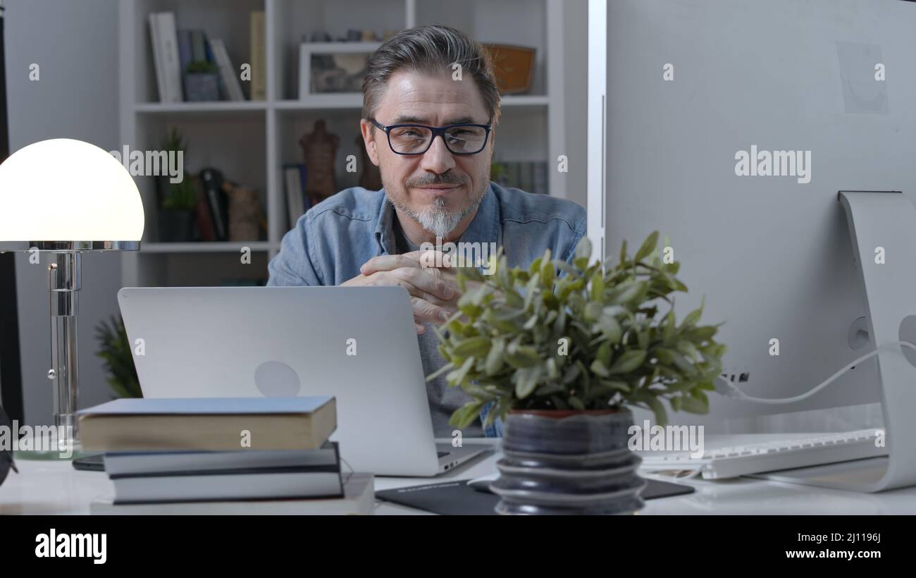 Portrait of happy older man in glasses sitting at desk working with ...