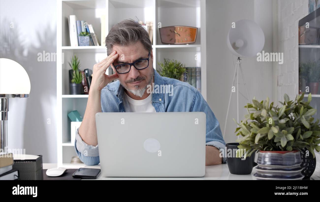 Older man working online with laptop computer at home sitting at desk ...