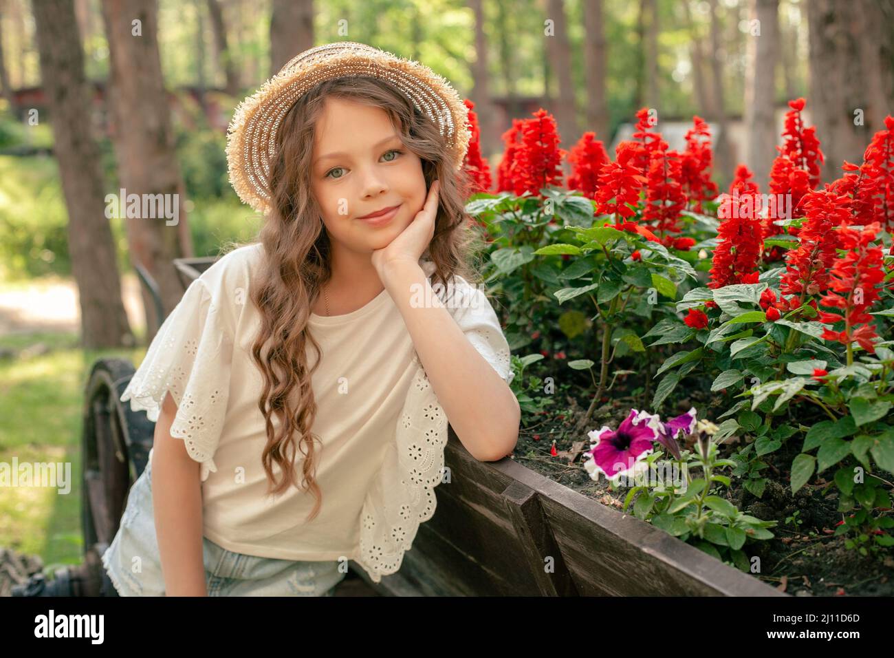 Dreamy cute tween girl sitting near flower bed with red salvia in ...
