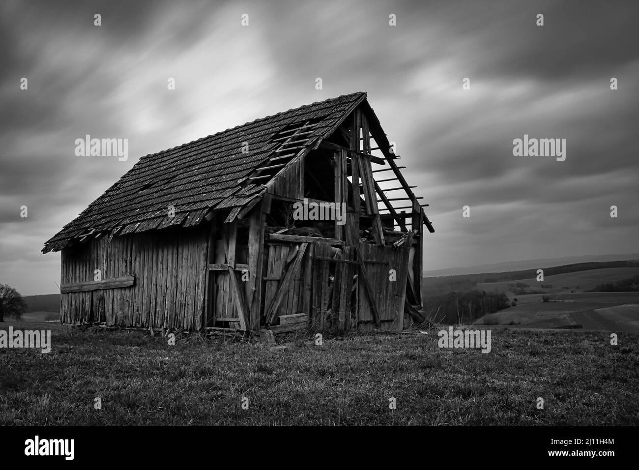 old spooky abandoned barn on a meadow with clouds in the background ...