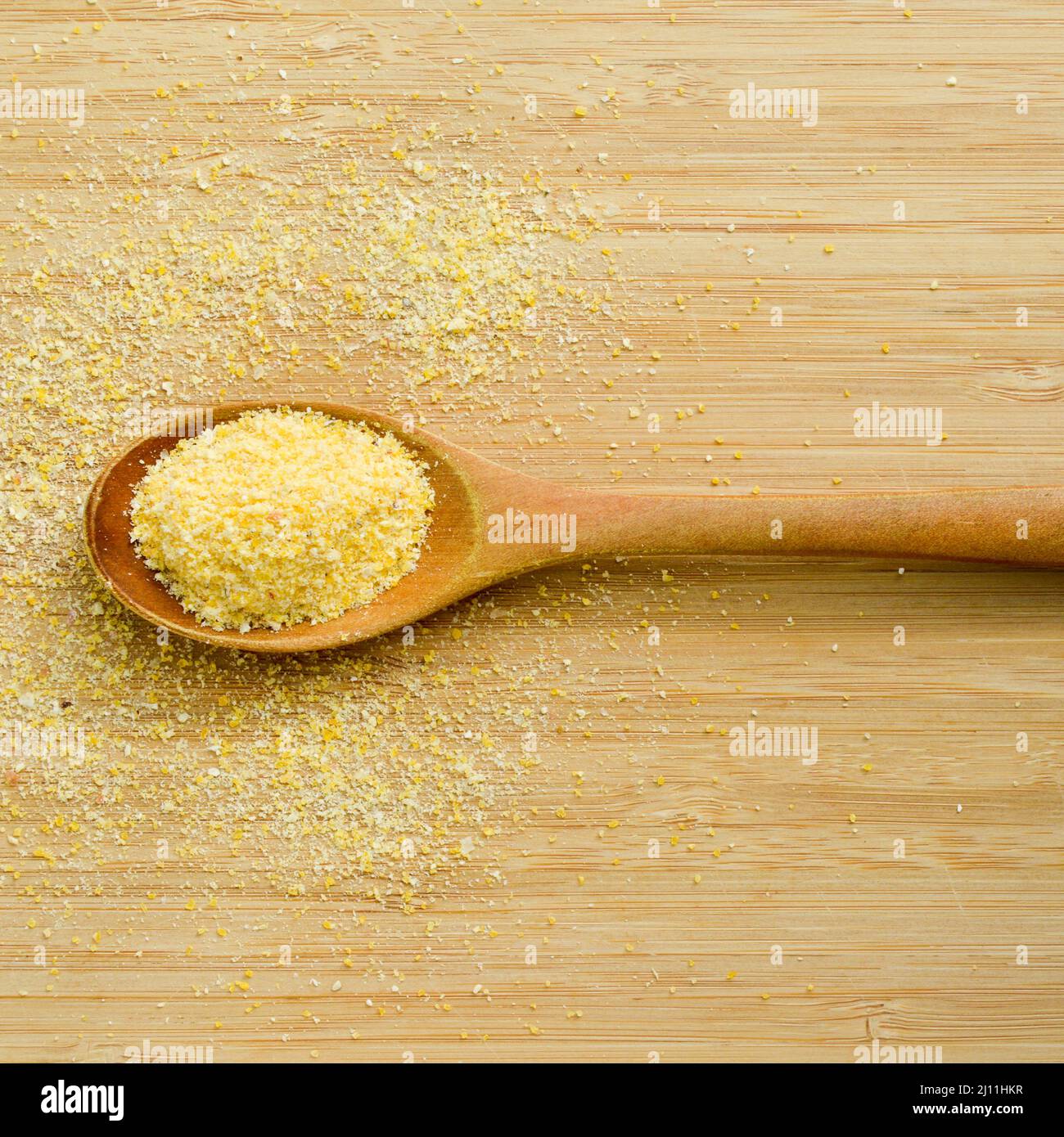 Uncooked yellow corn flour in wooden spoon on bamboo cutting board ...
