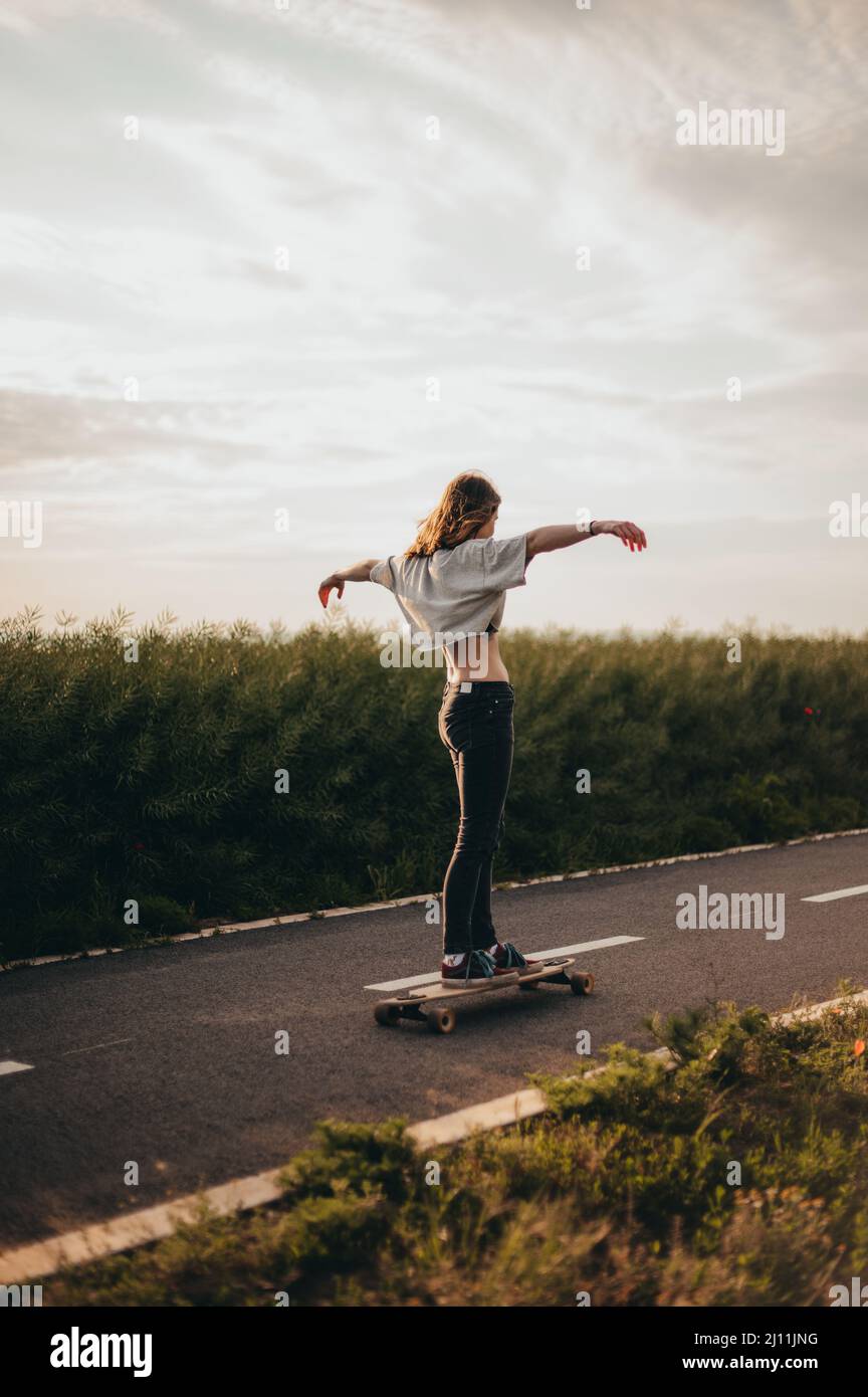 Girl rides a longboard with arms outstretched and enjoying a free ride ...