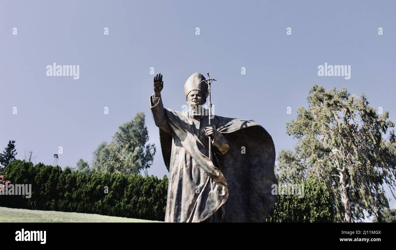 Statue of Pope John Paul II in the background of trees in the sunny day ...