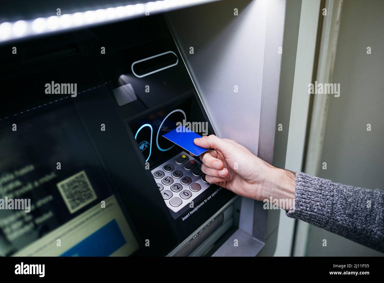 Close up of a man`s hand introducing a blue credit card to an ATM ...