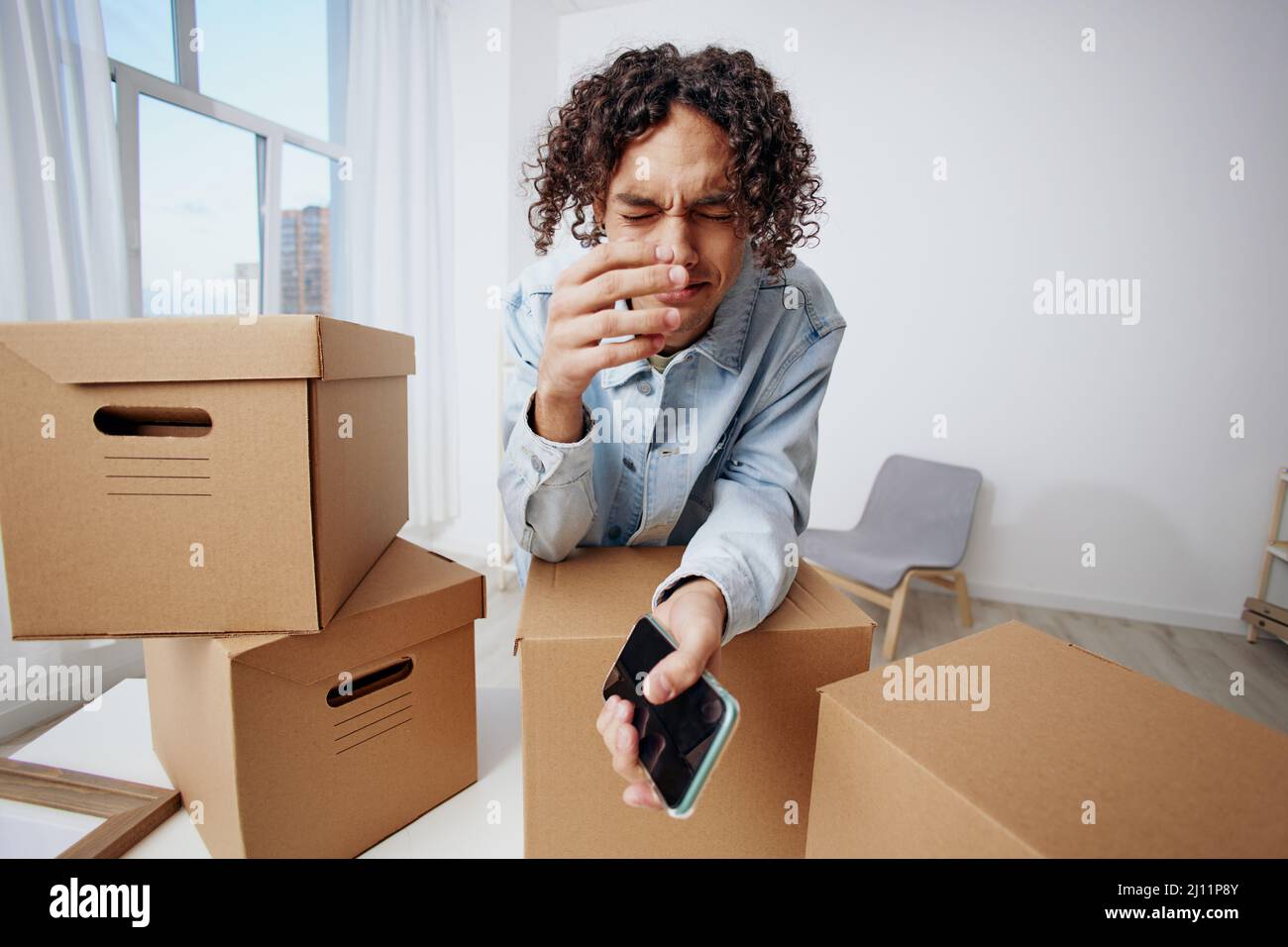 handsome guy with a phone in hand with boxes moving sorting things out ...