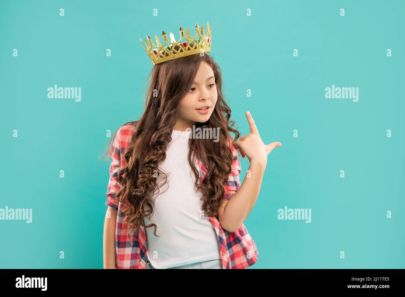 selfish child with curly hair pointing finger on queen crown on blue background, arrogance Stock ...