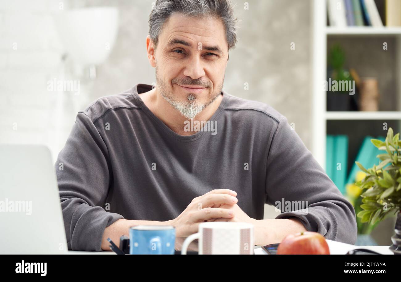 Portrait of man at home sitting at desk, working, looking at camera ...