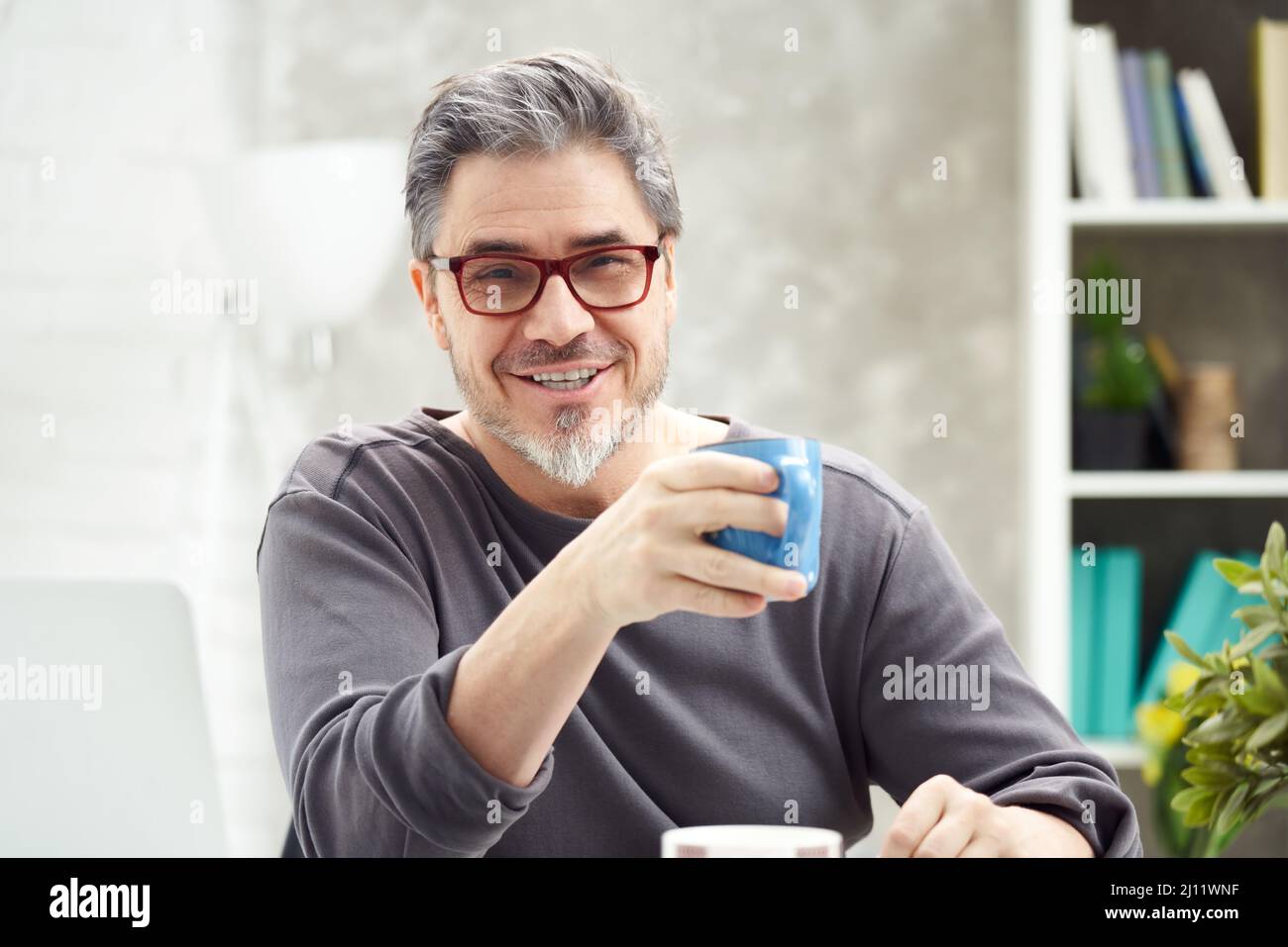 Portrait of happy man at home sitting at desk, working, looking at ...