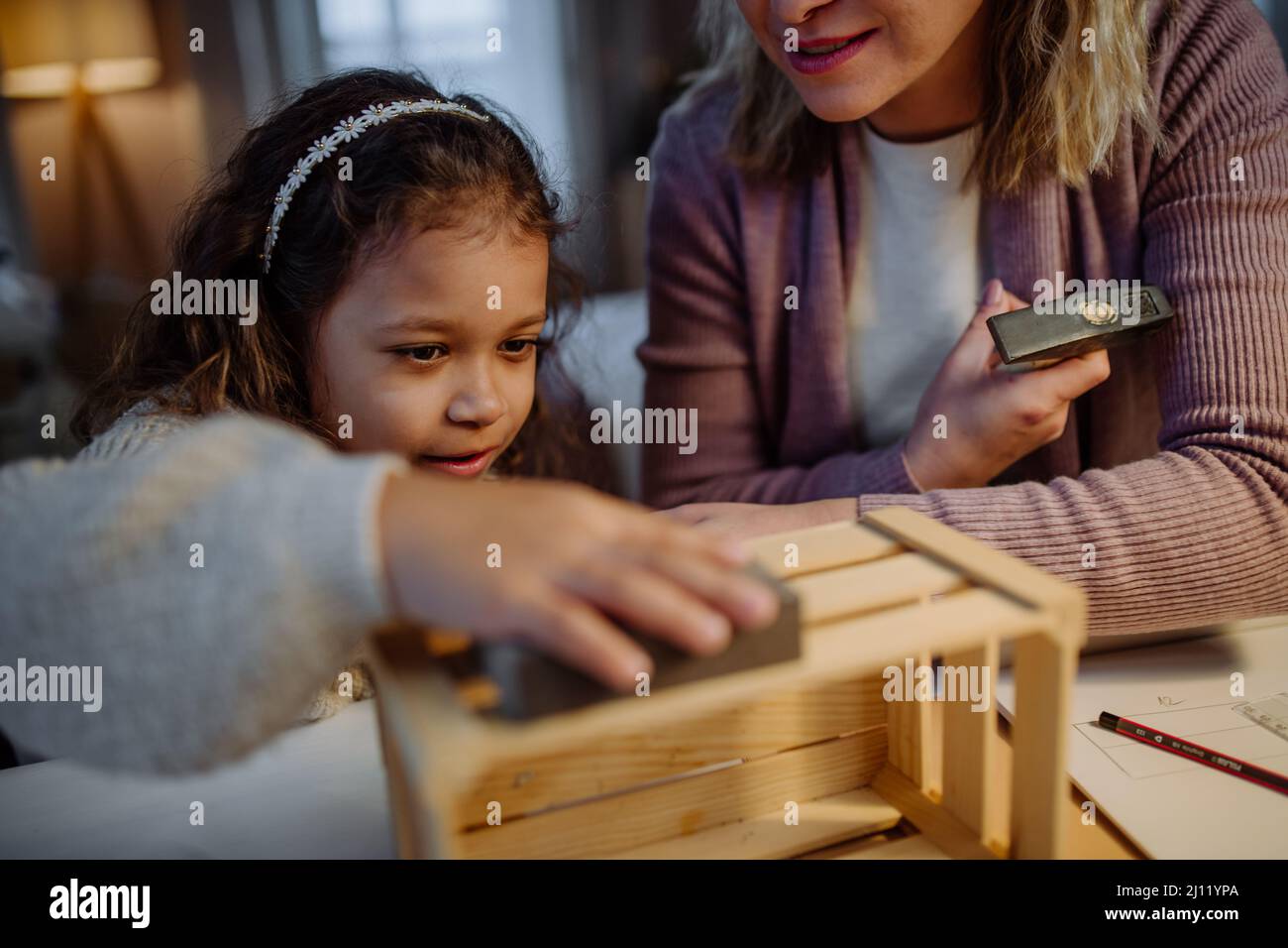 Happy little girl renovating a wooden crate together with her mother at ...