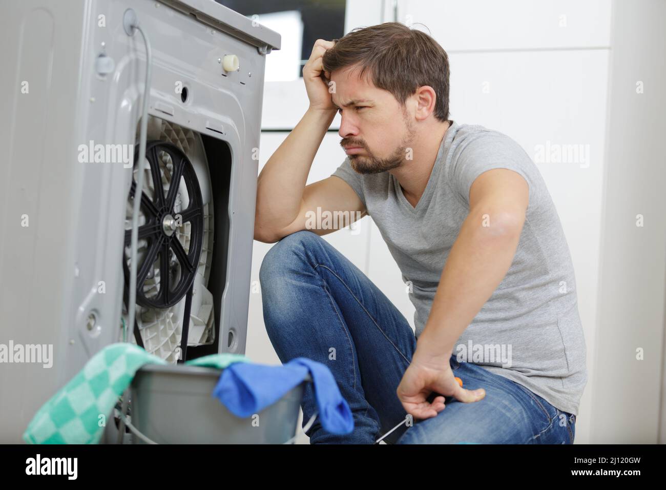 upset young man sitting next to washing machine Stock Photo - Alamy
