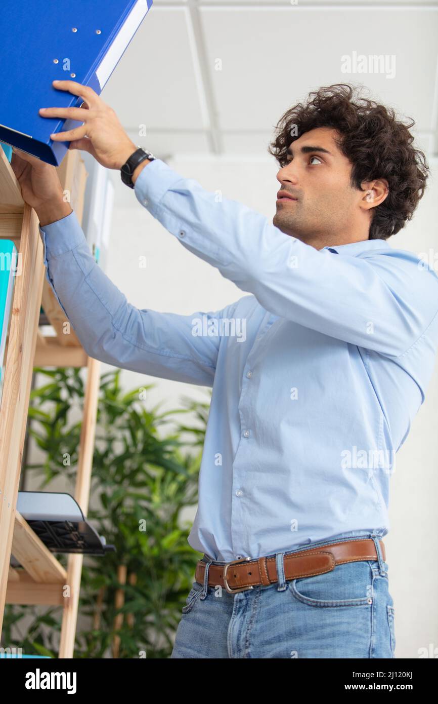 young man standing next to the shelf with folder Stock Photo - Alamy