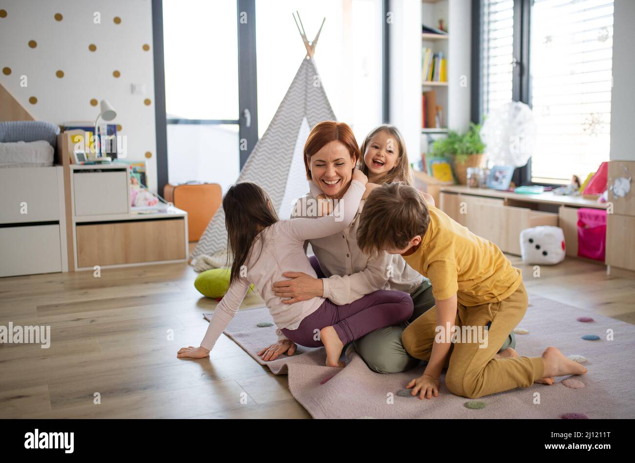 Cheerful mother of three little children receiving hugs from them at ...