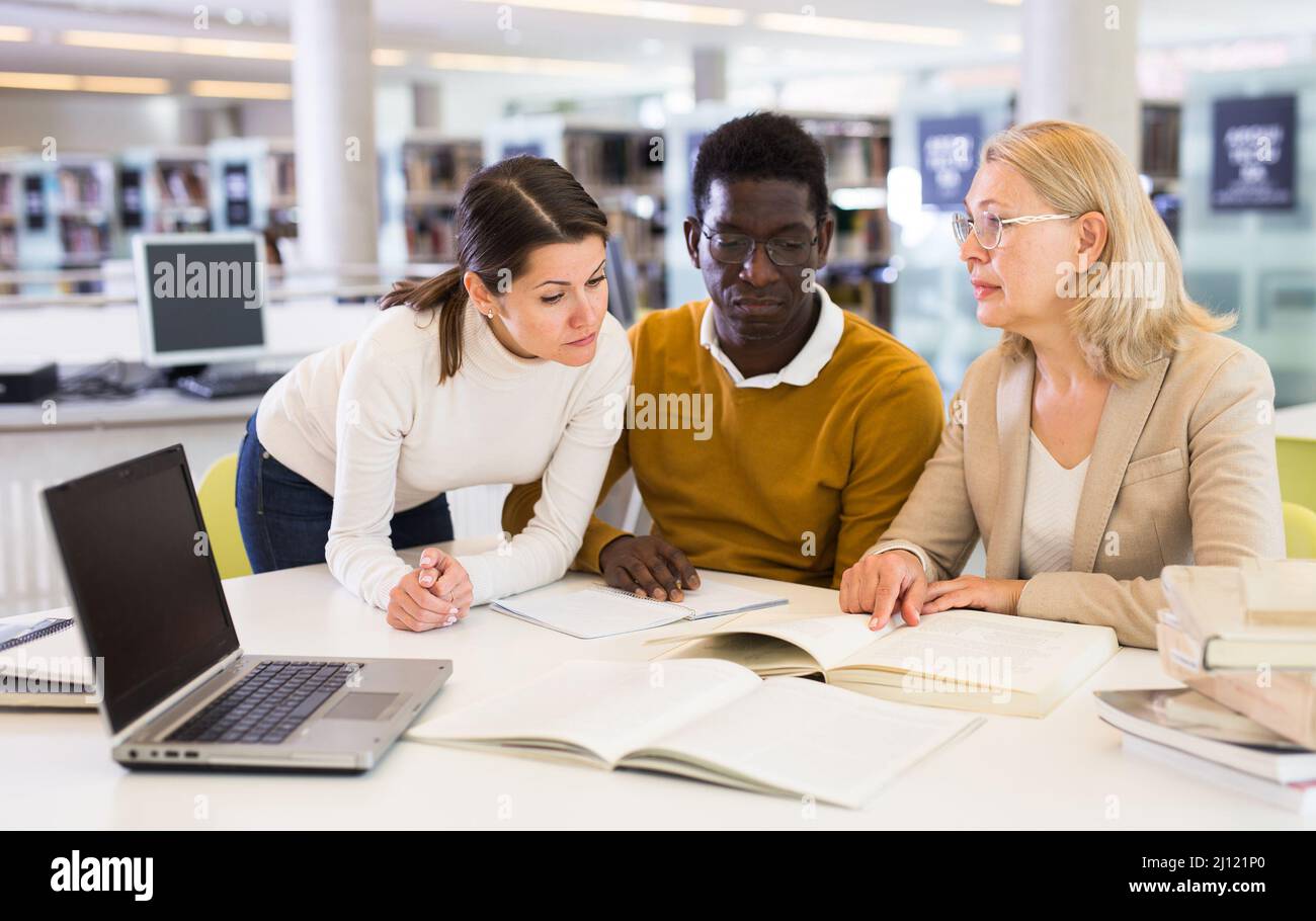 Students sitting in library, working with professor Stock Photo - Alamy