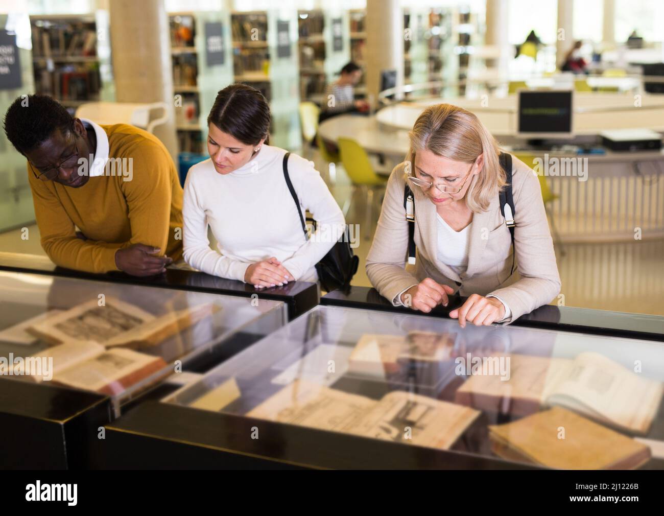 Teacher and adult students view rare books in a library showcase Stock ...
