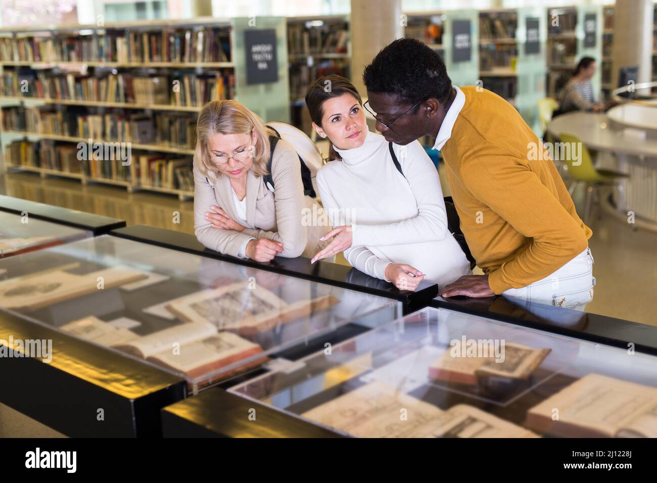 Professor and adult students read ancient books in a library showcase ...