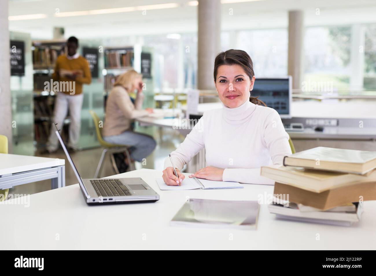 Adult female student with laptop and books in public library Stock ...