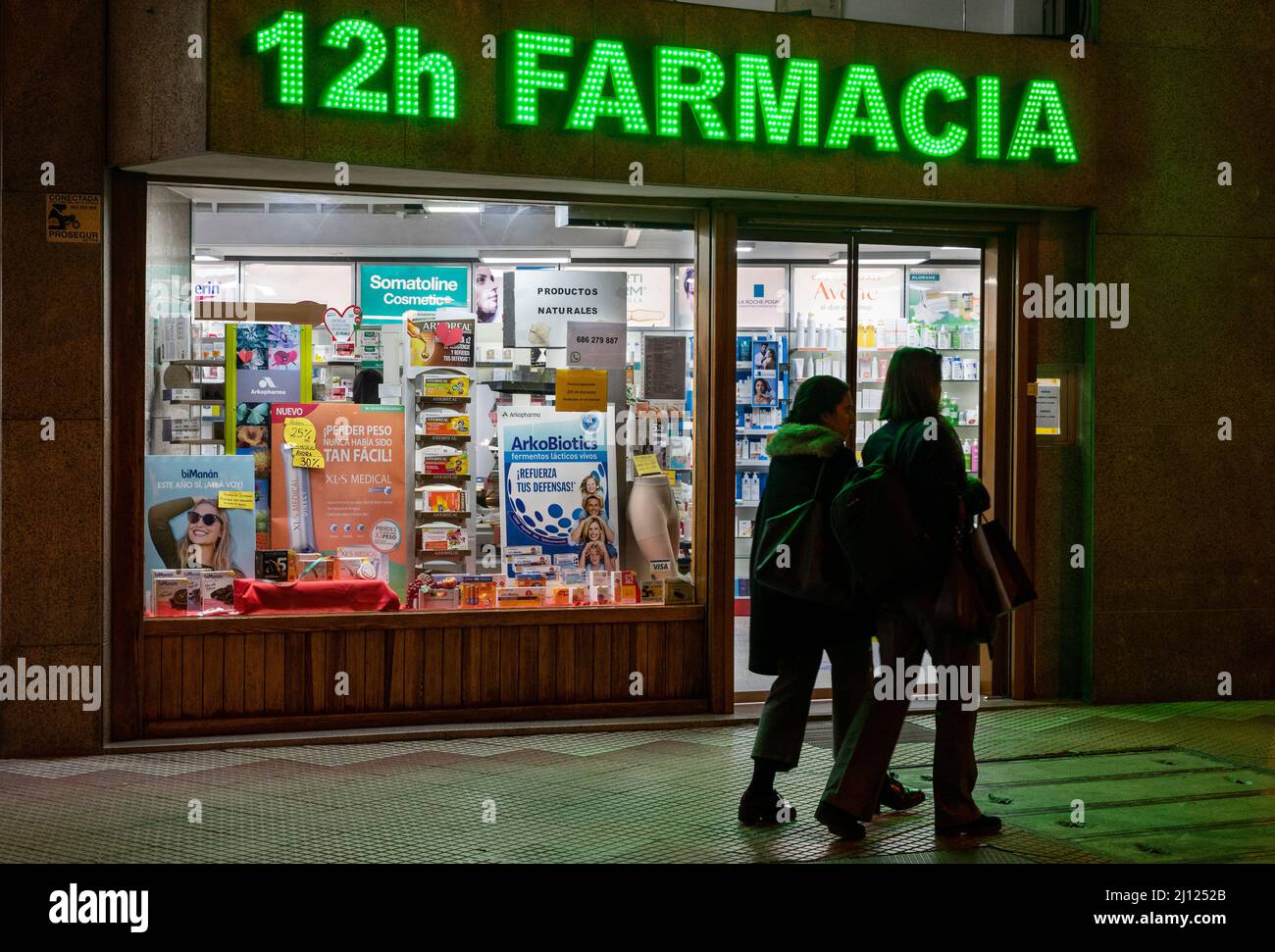 Pedestrians walk past a pharmacy, drugstore, during nighttime in Spain ...