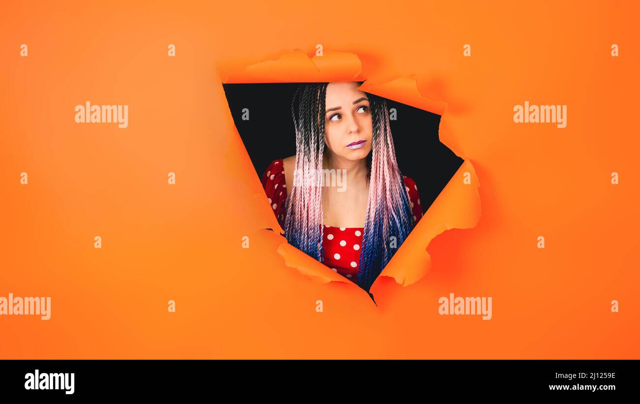 Young woman looking out of hole of orange background. Scared female ...