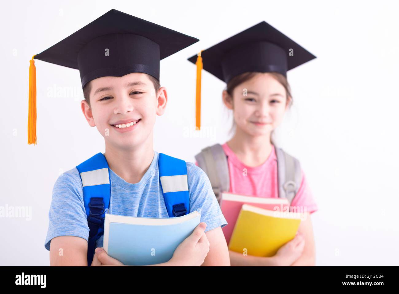 Happy boy and girl in graduation cap holding books Stock Photo - Alamy