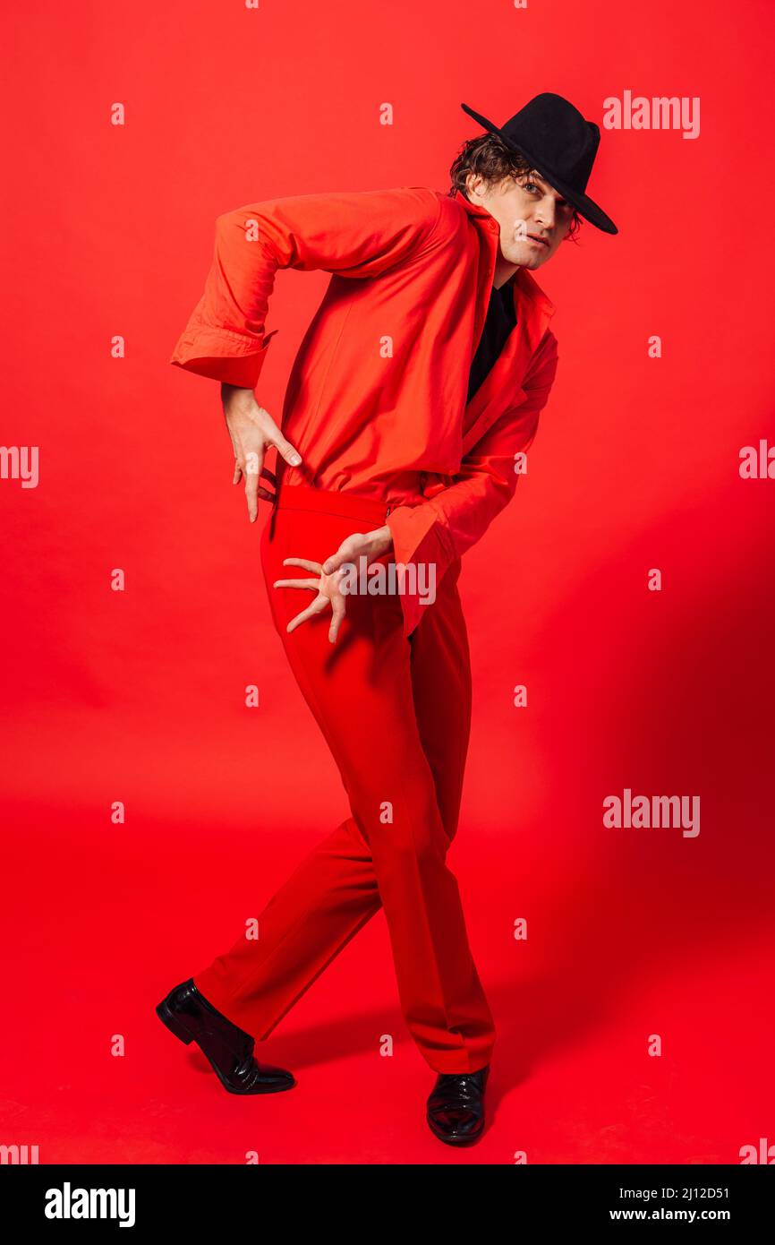 Tall handsome man dressed in red shirt and black hat posing on the red ...