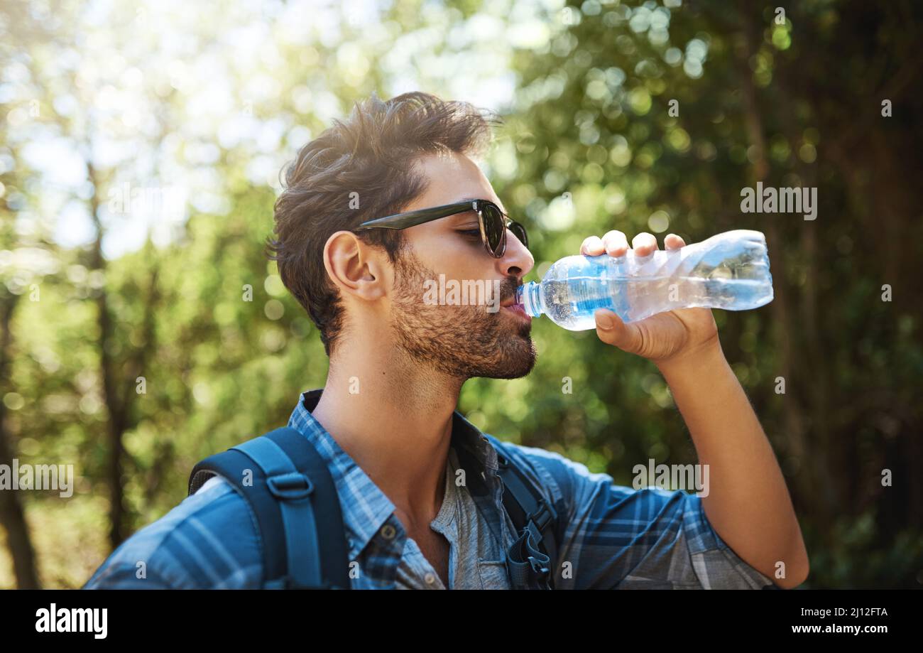 Staying hydrated on his hike. Shot of a young man stopping for a drink ...