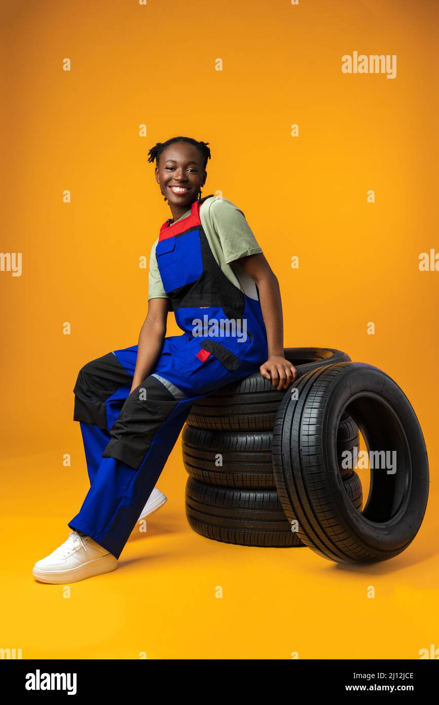 Portrait of smiling black female mechanic posing with new car tyres in ...