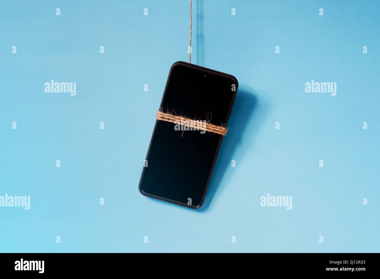 Old scrap cell phone hanging by a wire on a light blue background Stock ...