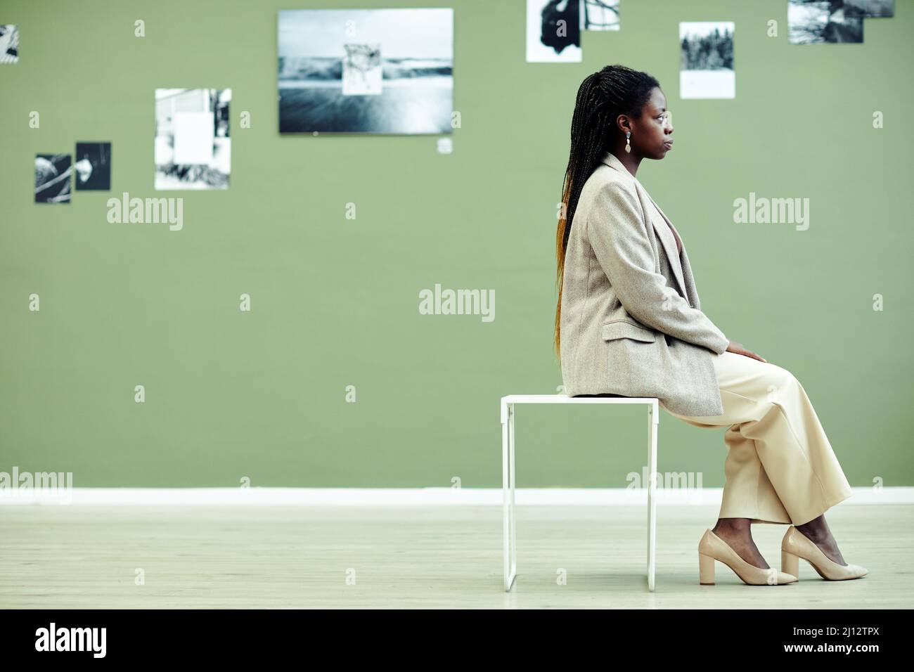 Side view of stylish young Black woman sitting on stool in modern art ...