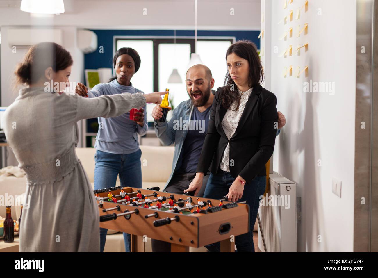 Happy workmates playing foosball game after work hours, having beer ...