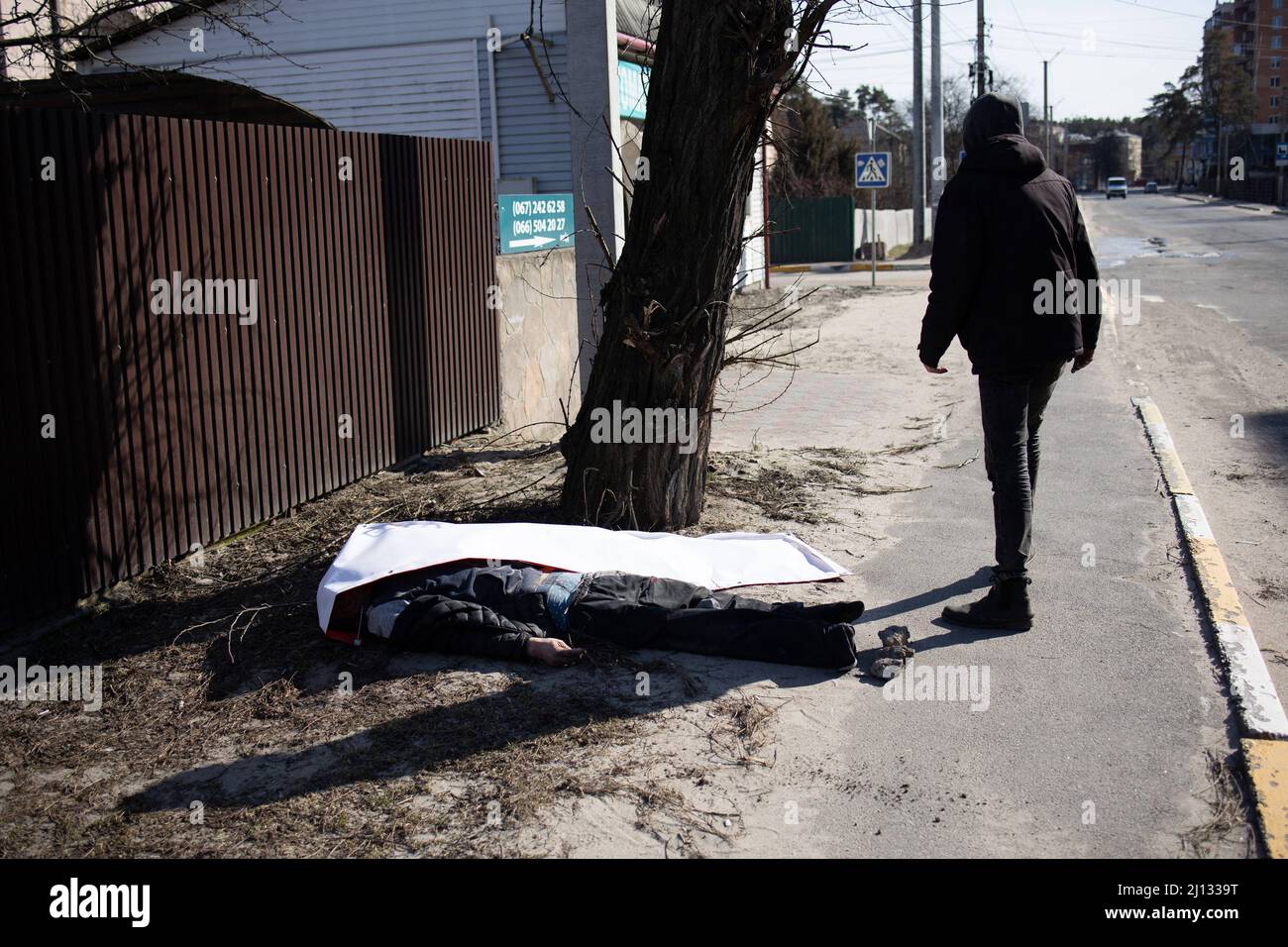 A man covers a corpse laying on the ground in a street of Central Irpin ...