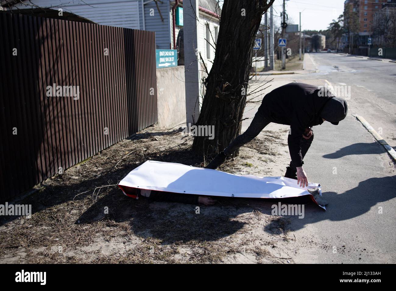 A man covers a corpse laying on the ground in a street of Central Irpin ...