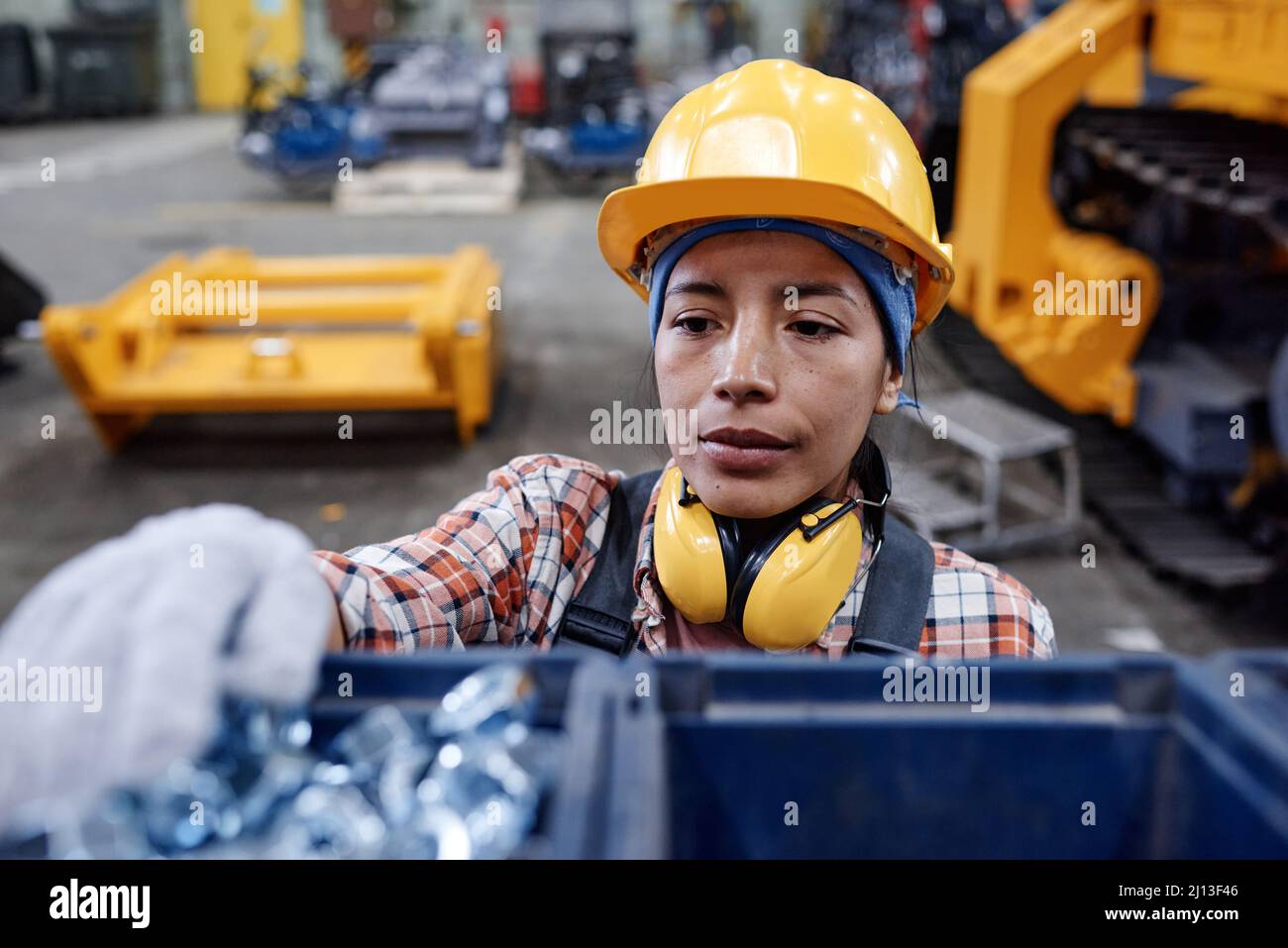 Young serious Hispanic female factory worker in gloves, hardhat and ...