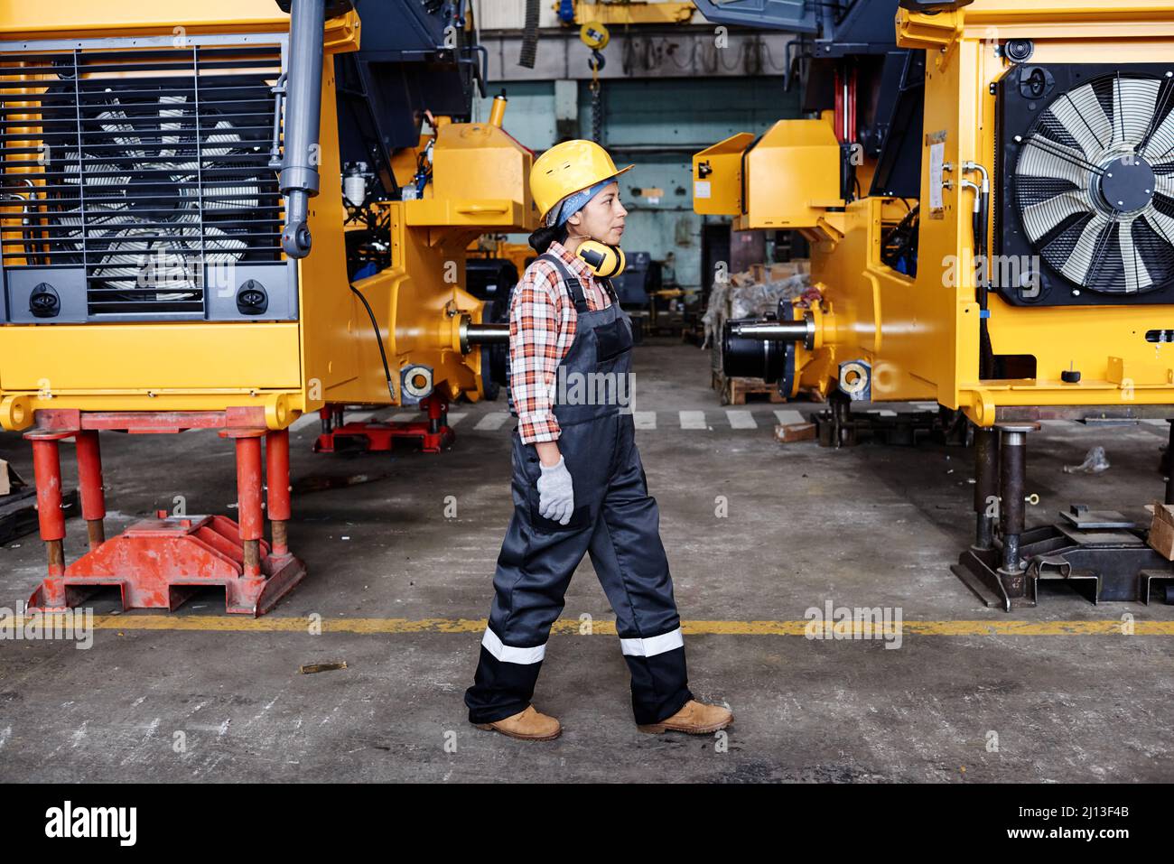 Young female technician in overalls, harhat and gloves moving along ...