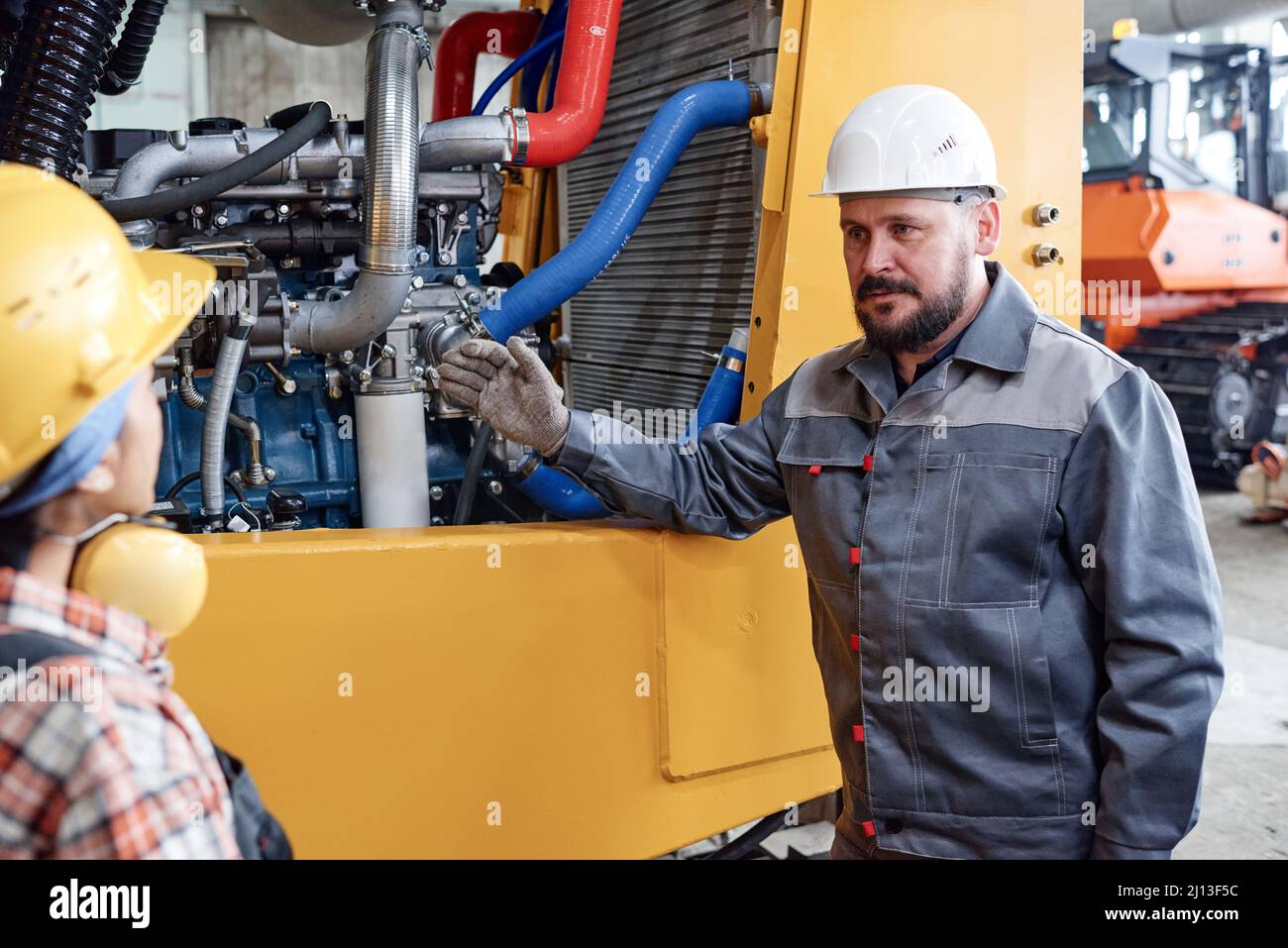Confident foreman in workwear consulting young female subordinate ...