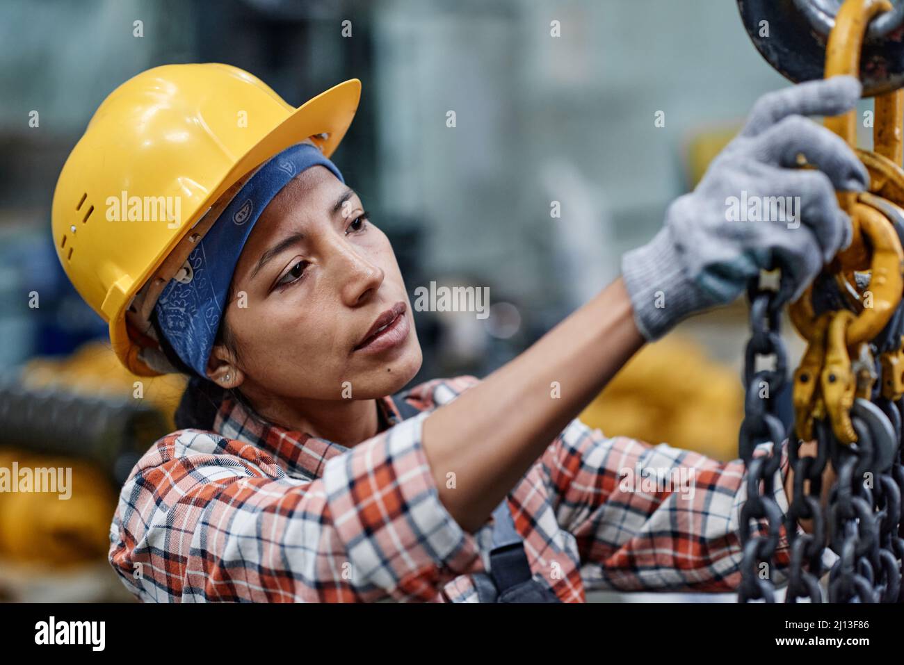 Young Hispanic female engineer in hardhat and gloves checking chains of ...