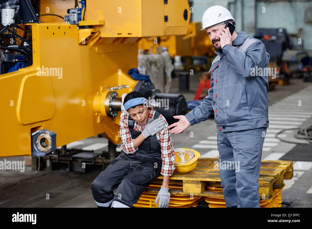 Mature worker of warehouse in workwear calling ambulance for his female ...