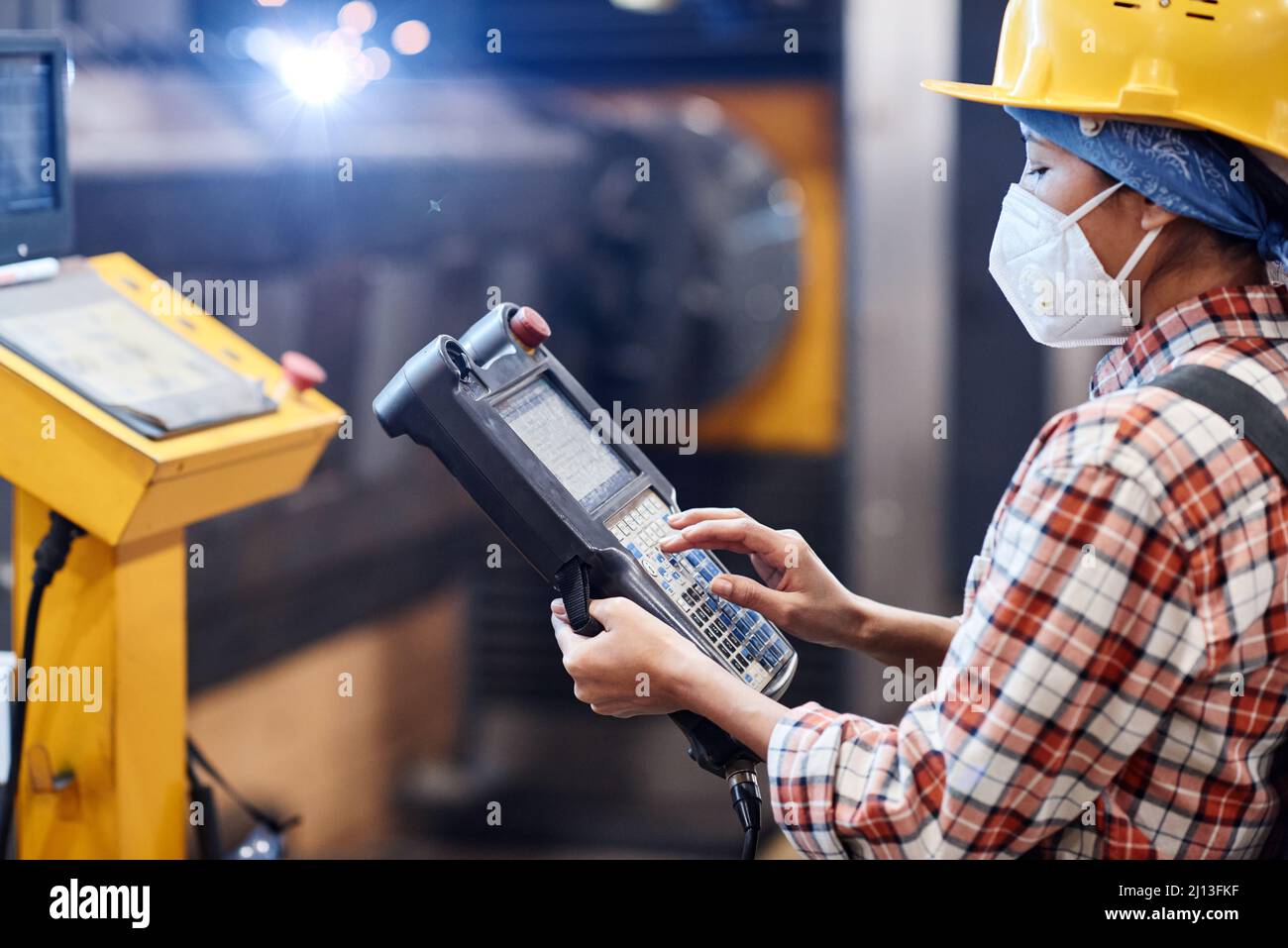 Female worker of plant in respirator and hardhat touching screen of ...